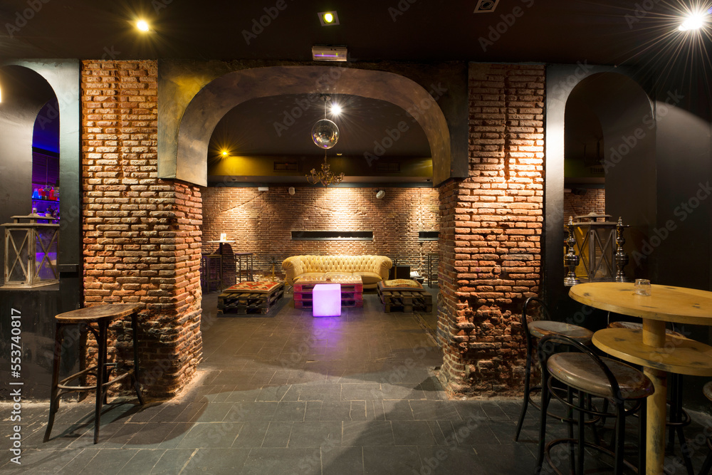 A late-night cocktail bar with vintage exposed brick walls, high tables ...