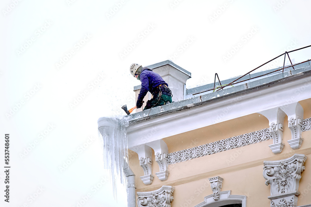 Man on roof with axe breakin icicle, removing ice from drainpipe ...