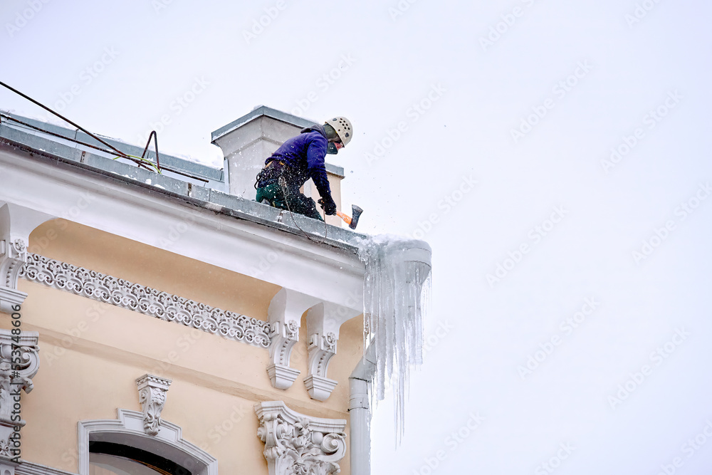 Worker on roof with axe breakin icicles, removing ice from drainpipe ...