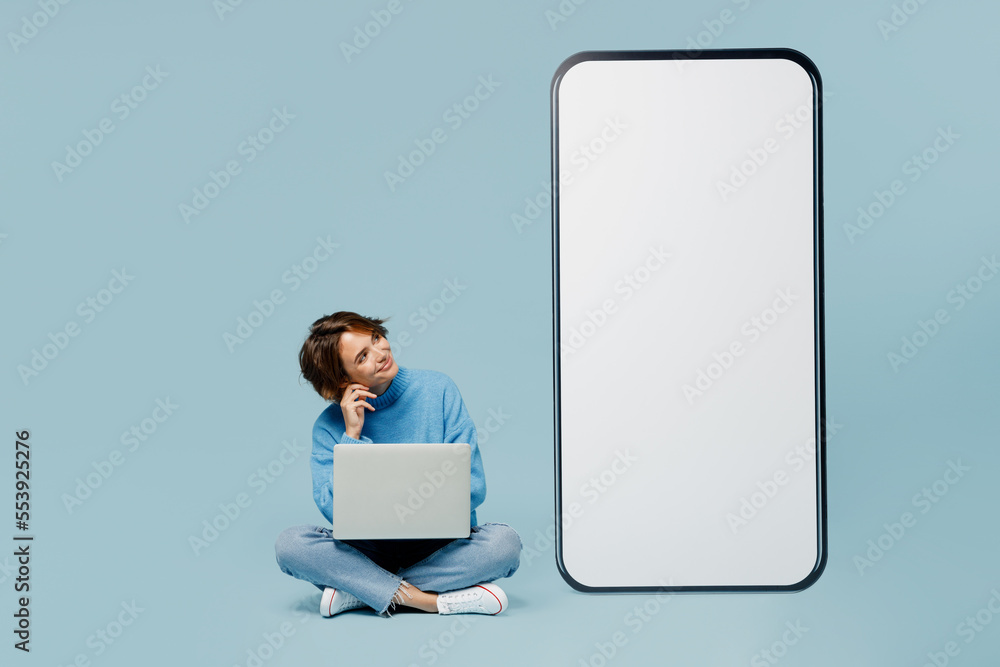 Full body young woman wears knitted sweater sit look at big huge blank ...