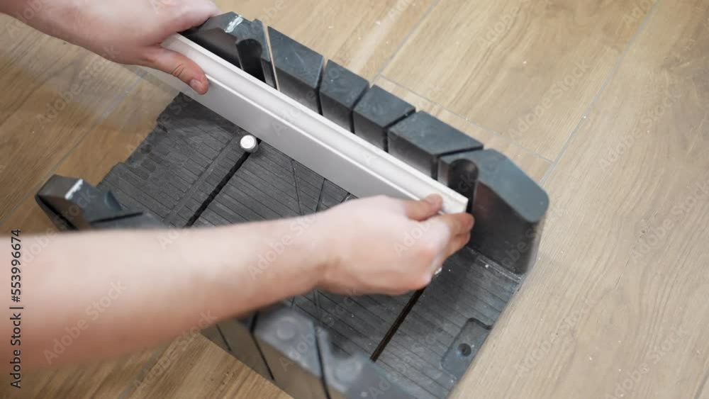 Workman measuring and fixing white plastic plinth for cutting and ...