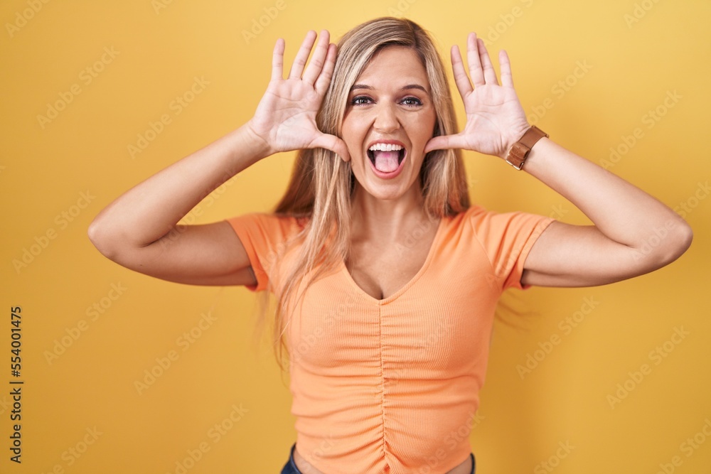 Young woman standing over yellow background smiling cheerful playing ...