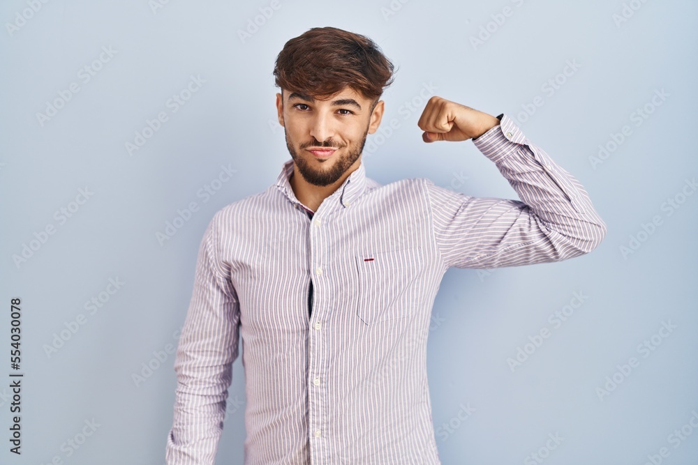 Arab man with beard standing over blue background strong person showing ...