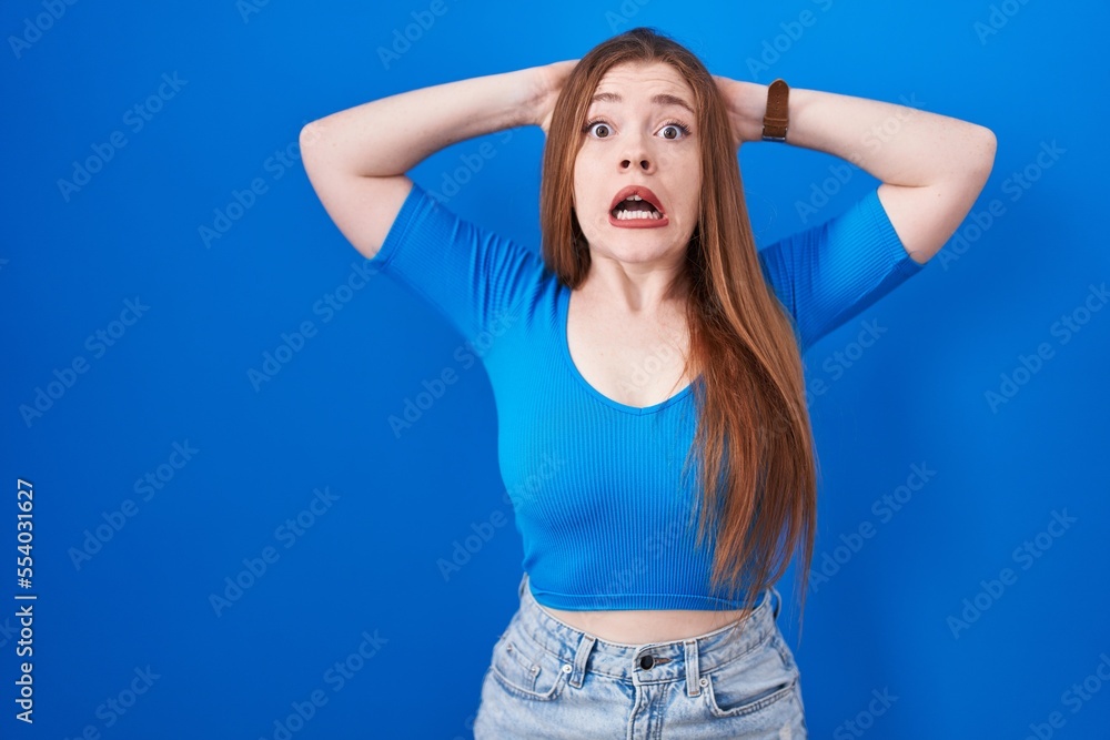 Foto de Redhead woman standing over blue background crazy and scared ...