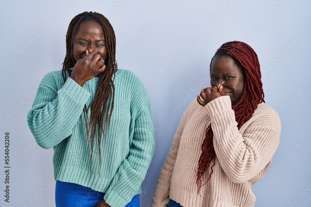 Two african woman standing over blue background smelling something ...