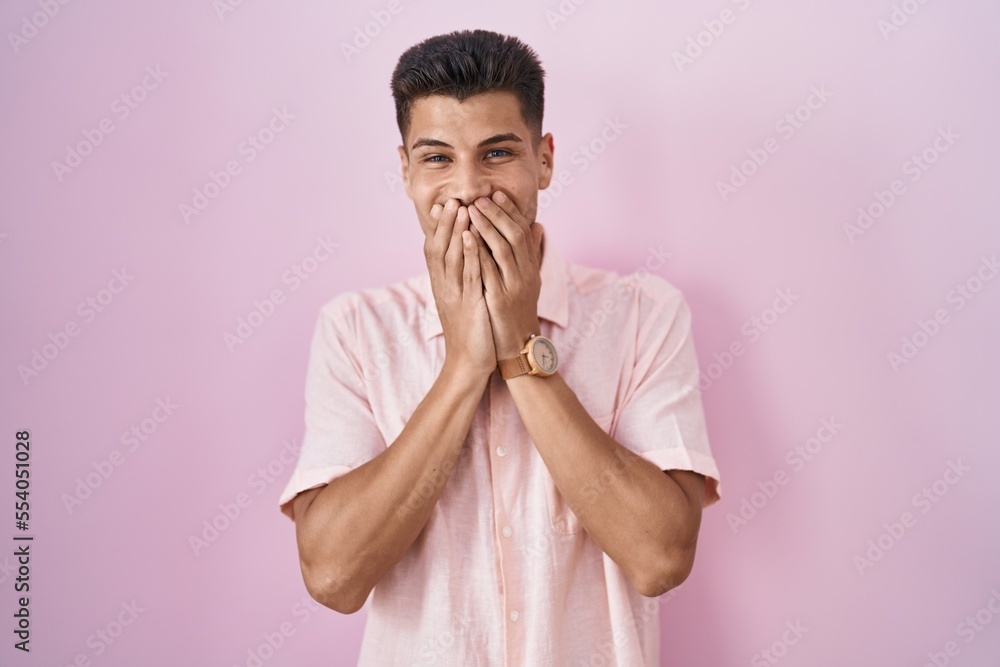 Young hispanic man standing over pink background laughing and ...
