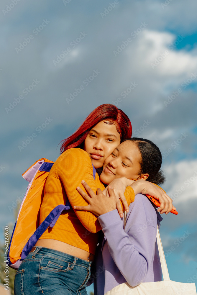 portrait of two Latina sisters hugging after school. Older sister ...