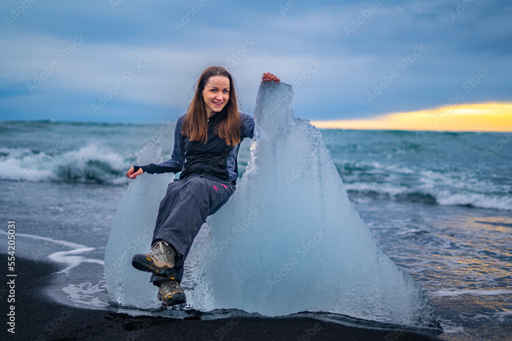 young woman sitting on big piece of ice with raised on hand up at ...