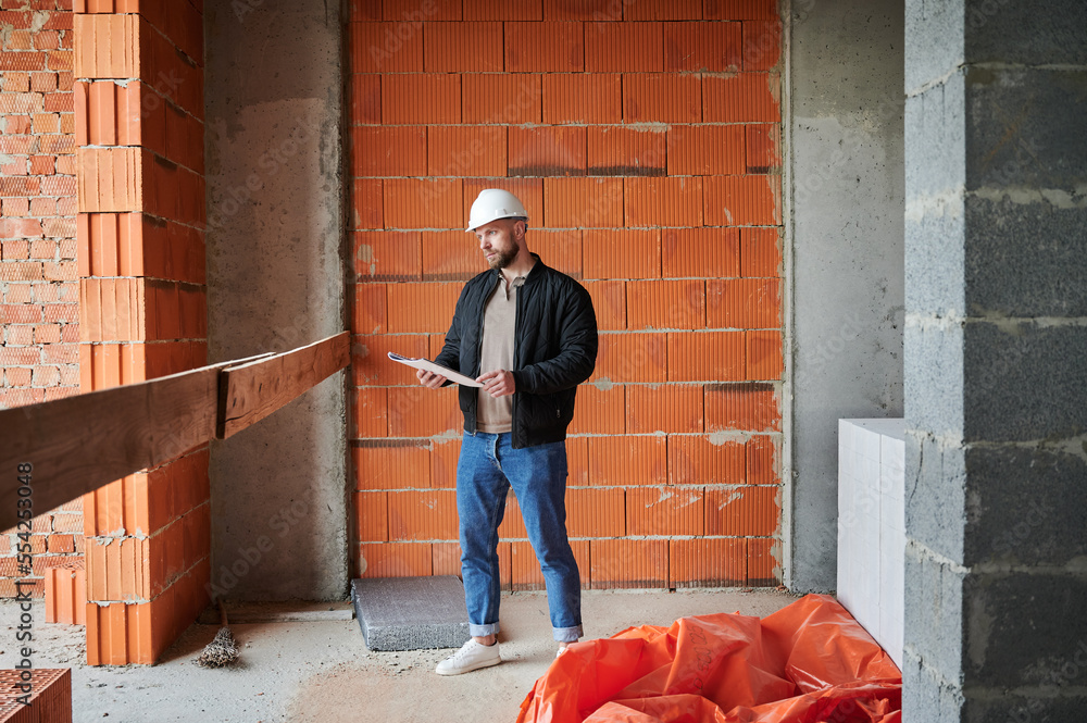 Full length of man worker in safety helmet holding papers and looking ...