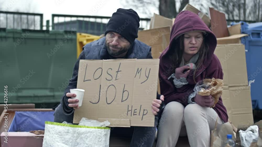 Two sad homeless men sit by the rubbish bins. Man and a woman are poor ...