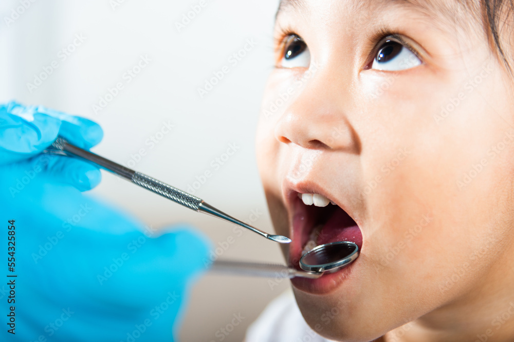 Dental kid health examination. Doctor examines oral cavity of little child uses mouth mirror to ...