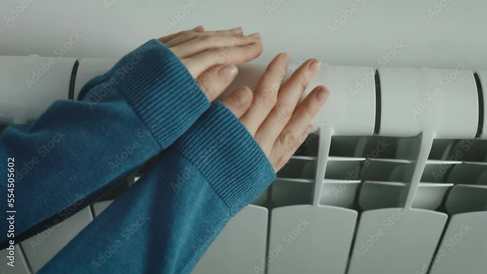 Women's hands touch the heating radiator in the apartment. The woman is ...