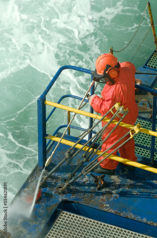 Seafarer working on a deck of a container vessel with a water jet ...