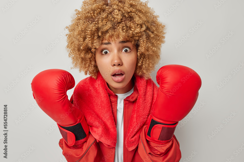 Shocked curly haired female boxer has strong opponent wears red boxing ...
