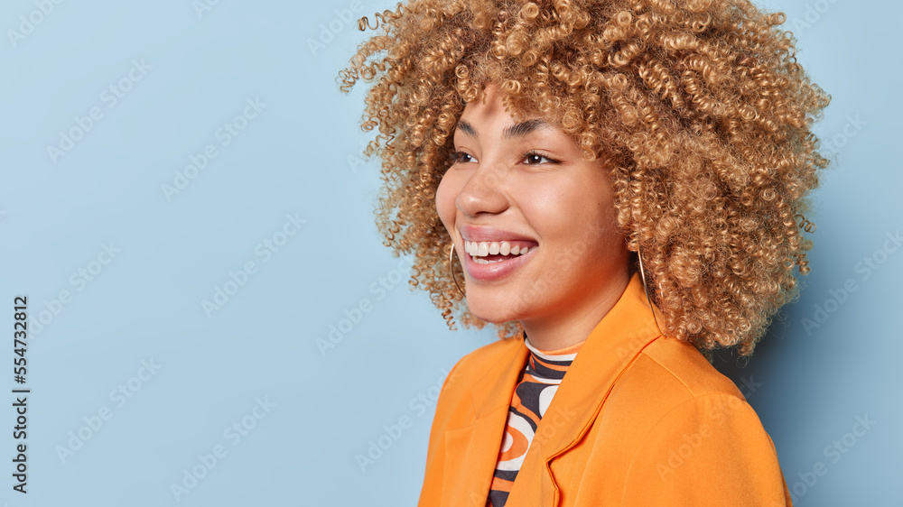Sideways shot of happy curly haired young woman smiles broadly glad to ...