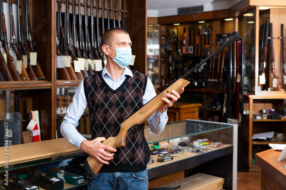 Portrait of gun store owner wearing medical face mask demonstrating ...