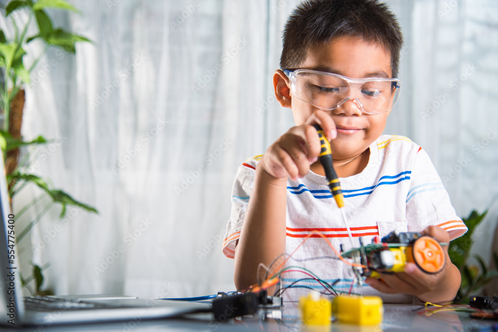 Asian kid boy assembling the Arduino robot car homework project at home, Little child tighten ...