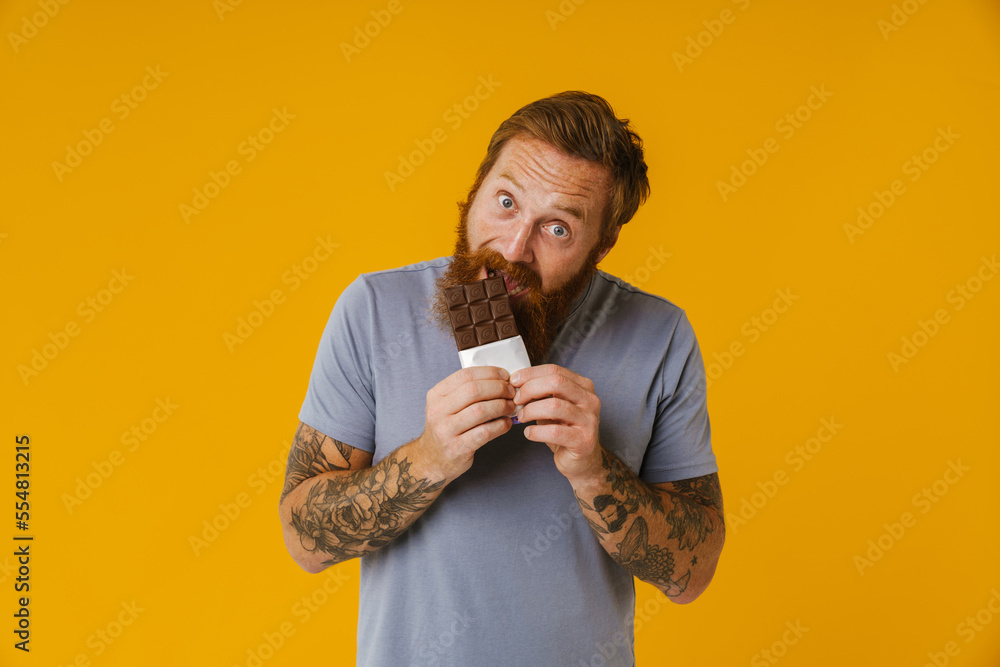 Bearded happy man eating chocolate bar while standing isolated Stock ...