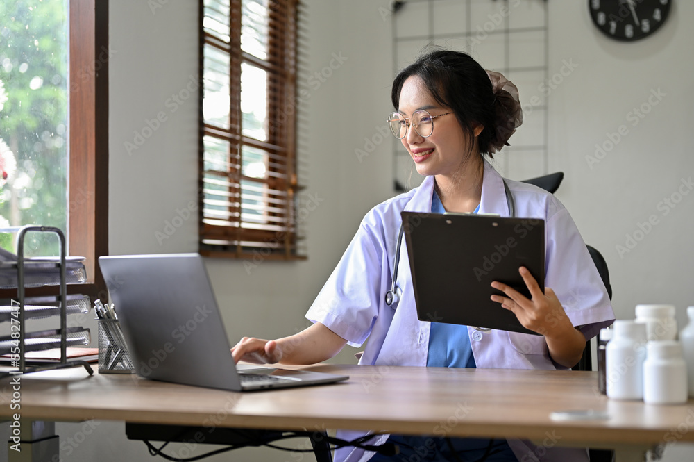 Beautiful Asian female doctor using laptop computer, working at her ...