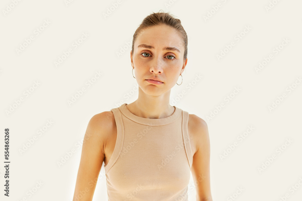 Sad depressed young girl standing alone in beige tank top looking at ...
