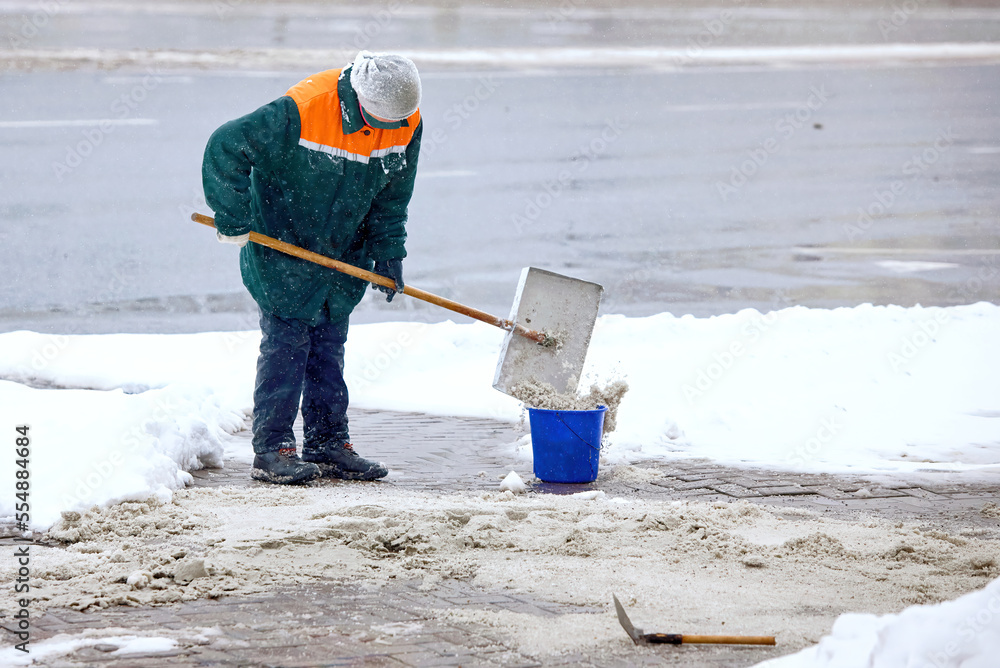 Worker pour rock salt into bucket with shovel to treat snowy sidewalk ...
