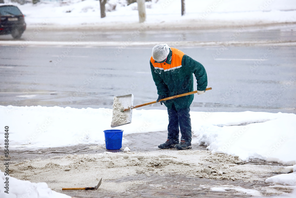 Worker pours salt reagent into bucket with shovel to treat snowy ...