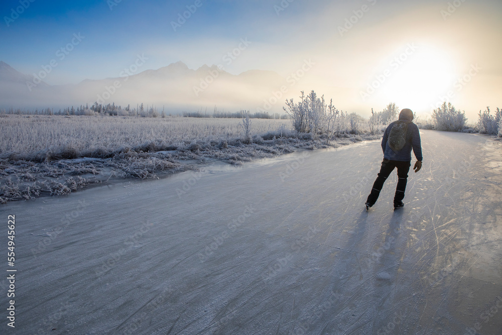 Man backcountry ice skating on Rabbit Slough with frosty fog and bright ...