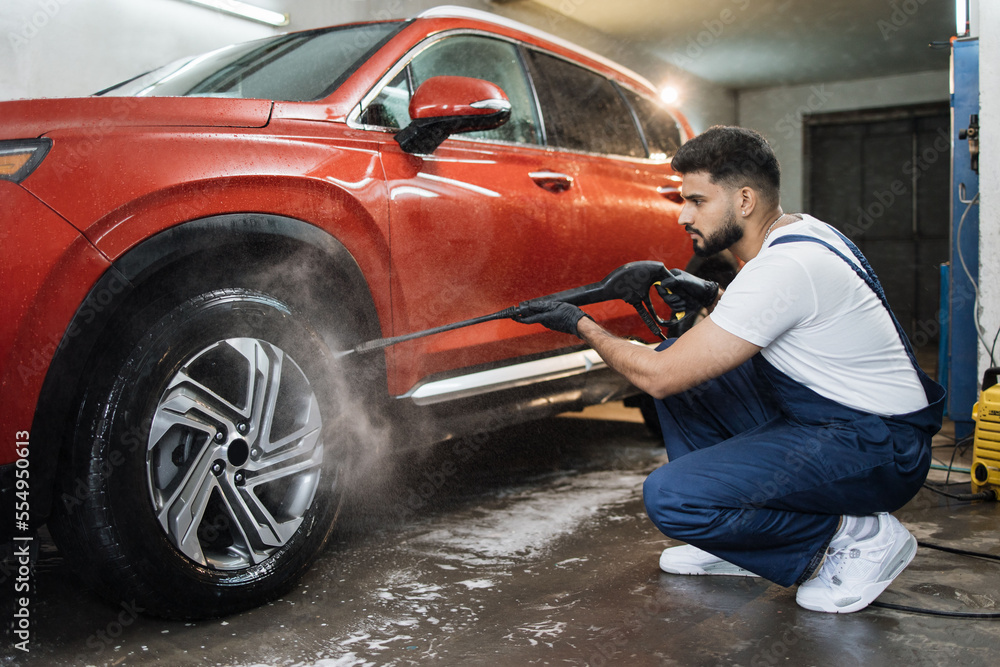 Side view portrait of young bearded male worker washing the car wheels ...
