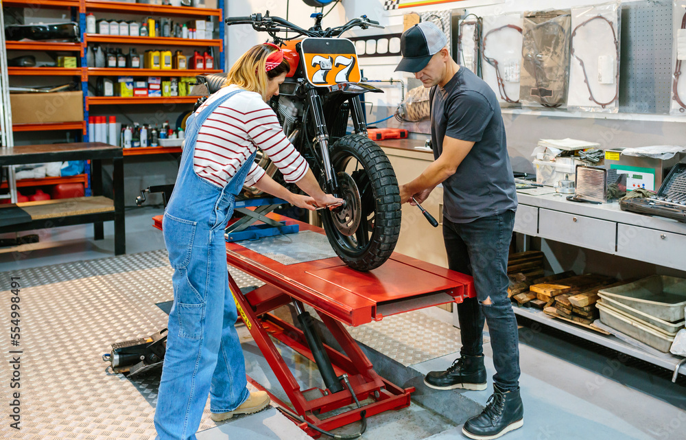 Mechanic couple team adjusting motorbike wheel over platform on factory ...