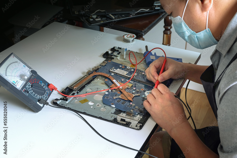 computer technician A laptop motherboard repairman is using an IC meter ...