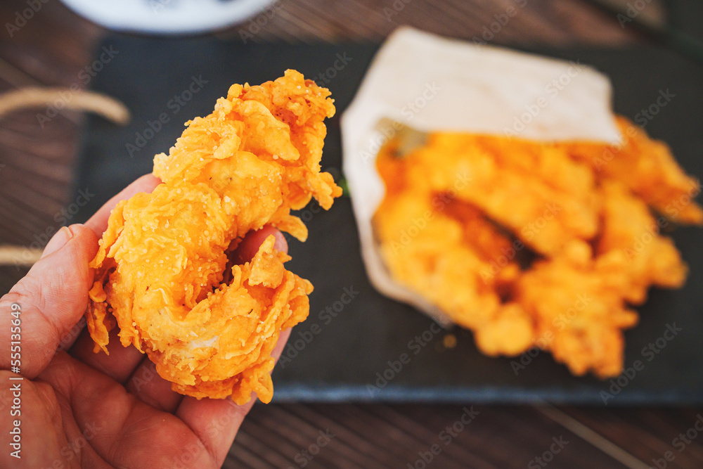 arm and meat strips on a black tray. strips of meat fried in breading ...