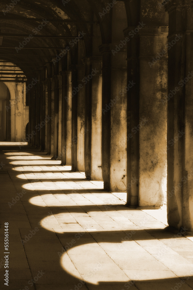 Walkway with shadows of arches and columns on the ground cast by bright ...