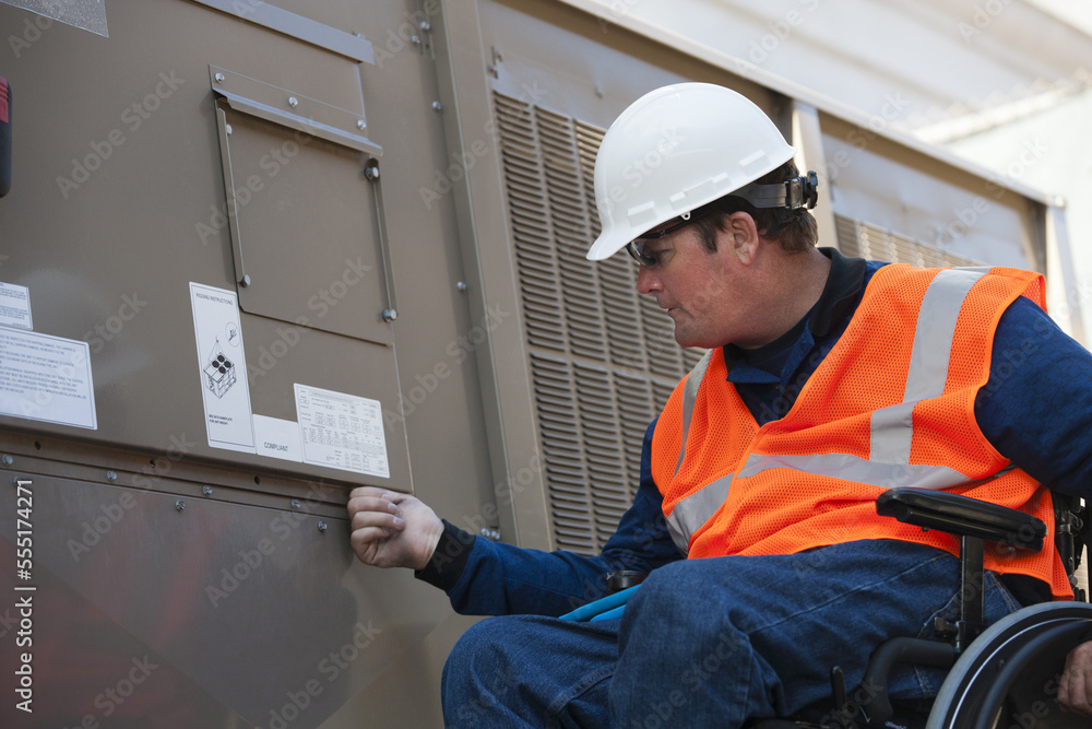 Facilities engineer in a wheelchair opening inspection plate of ...