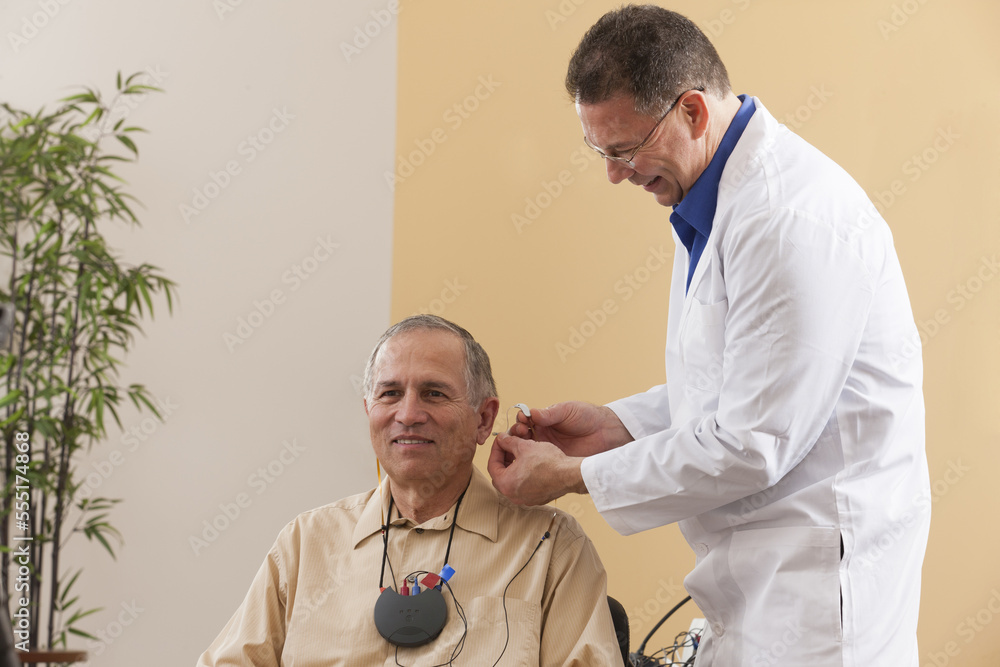 Audiologist inserting behind-the-ear hearing aid into a patient's ear ...