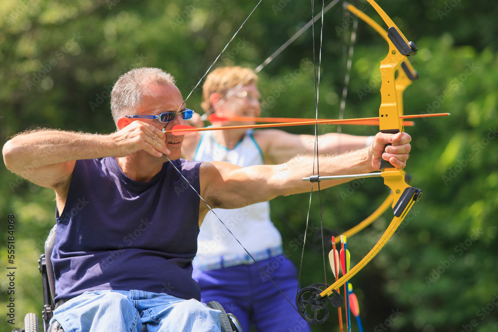 Man with spinal cord injury and woman with prosthetic leg aiming arrows ...