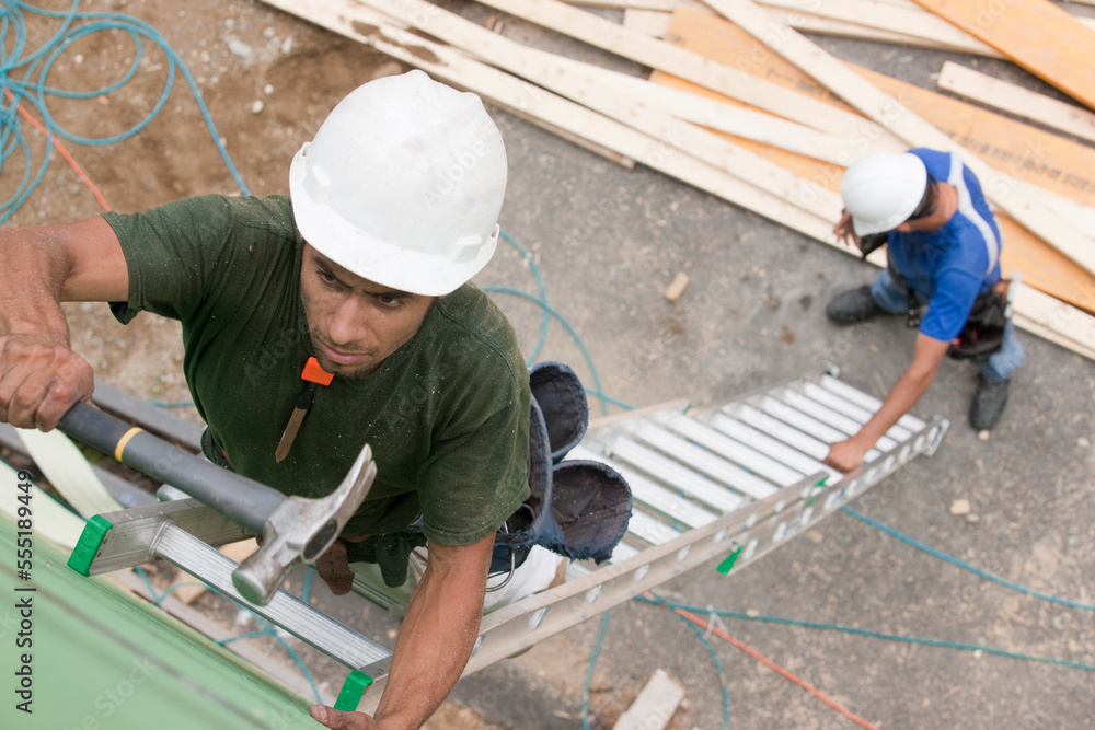 Carpenters on an extended ladder for installing sheathing at a ...