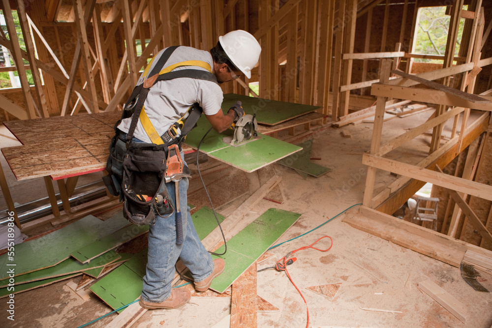 Carpenter using a circular saw on exterior wall sheathing in a house ...