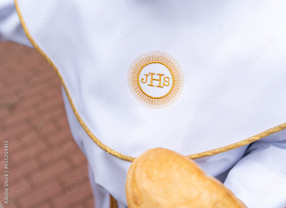 First Communion child in white alb with IHS badge holding bread with a ...