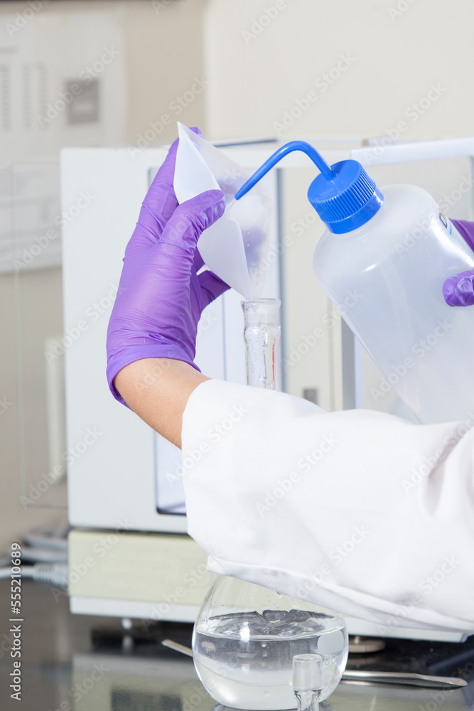 Laboratory scientist washing solid reagent into a water sample in a ...