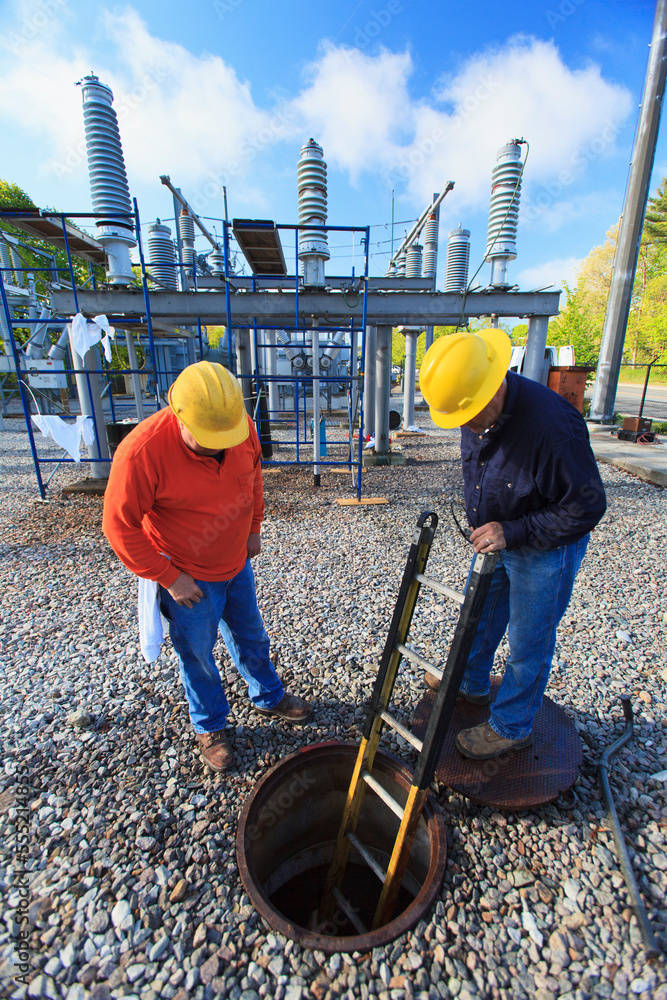 Power engineers looking inside manhole at high voltage power ...