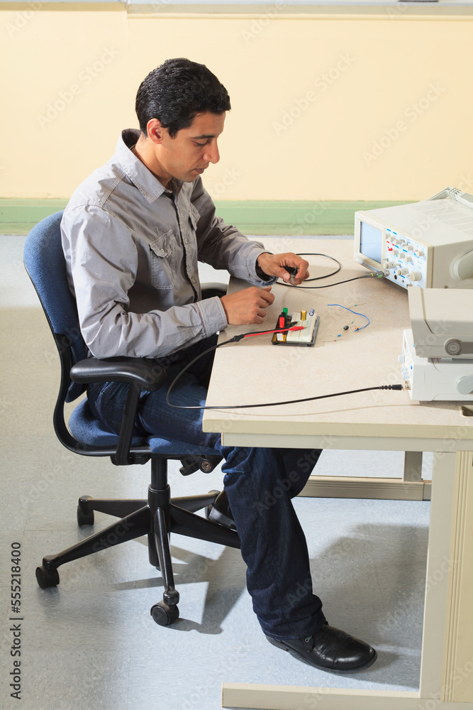 Engineering student connecting oscilloscope to measure prototyping breadboard for an electronics ...