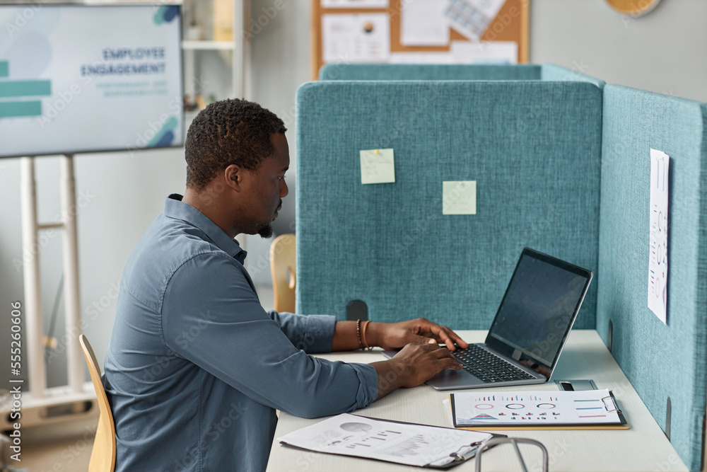 Side view portrait of black man working with laptop at workplace ...