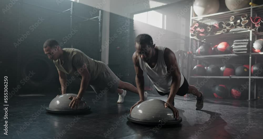 Two muscular fit African-American men working out in modern gym with equipment doing push ups on ...