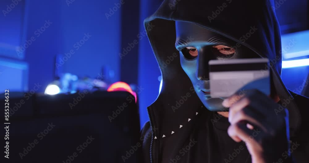 A hacker wearing a mask to cover his face is using computer to hack ...