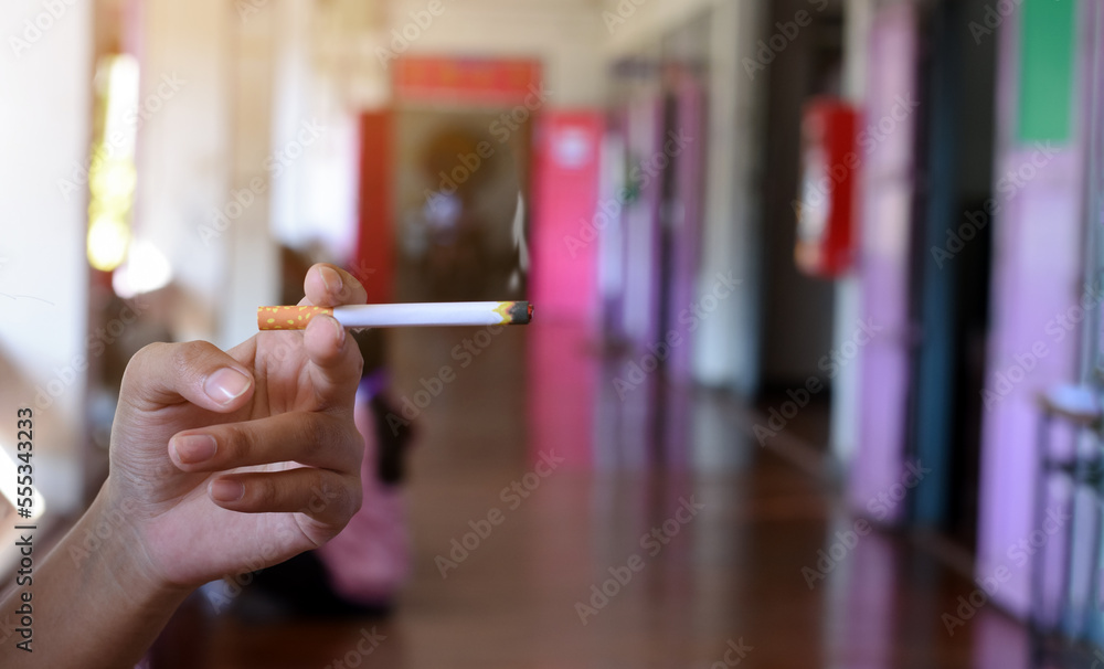 Closeup hand holding cigarette with blurred front balcony of classroom ...