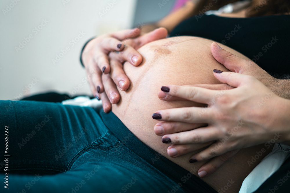 Hands of expectant parents caressing baby bump. Fingers intertwine as ...