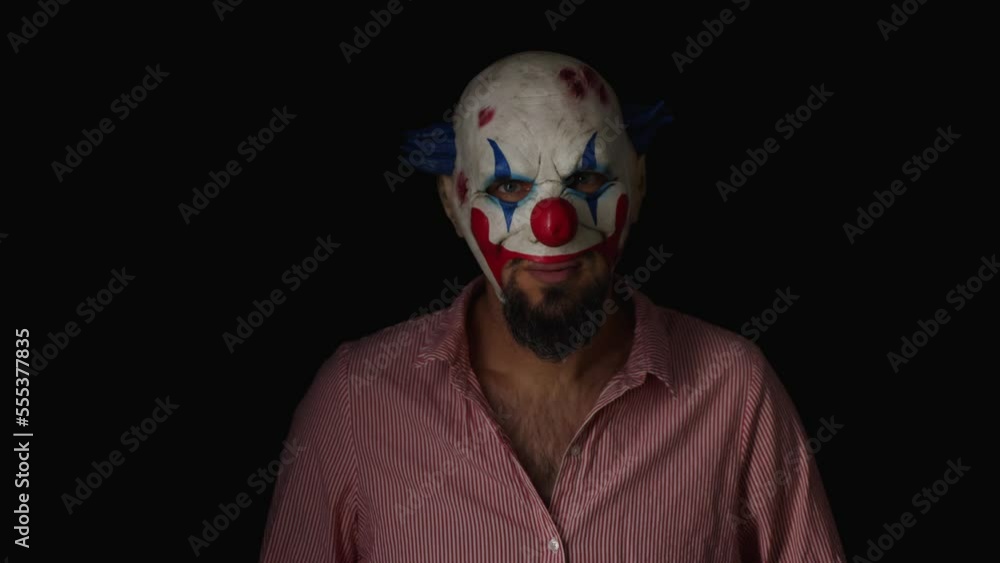 A bearded man wearing a scary evil clown mask jumps abruptly out of the ...