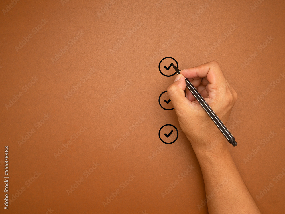 Hand holding a pen check-marking on the checklist box on a brown ...