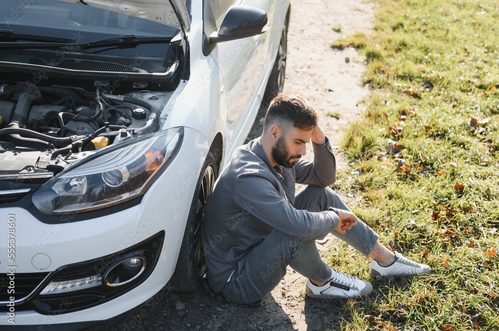 Frustrated sad upset guy driver is sitting near a broken car after road ...