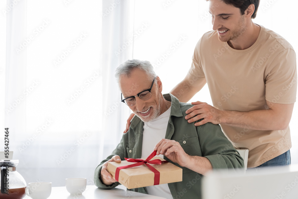 smiling guy touching shoulders of pleased dad opening fathers day ...